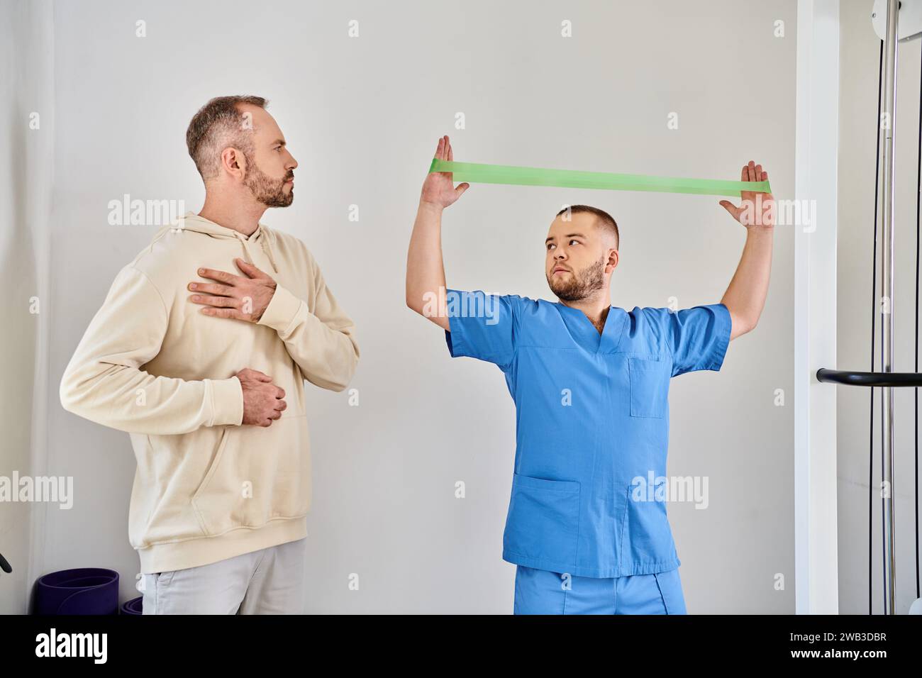 rehabilitologist showing exercise with resistance band to man with ...