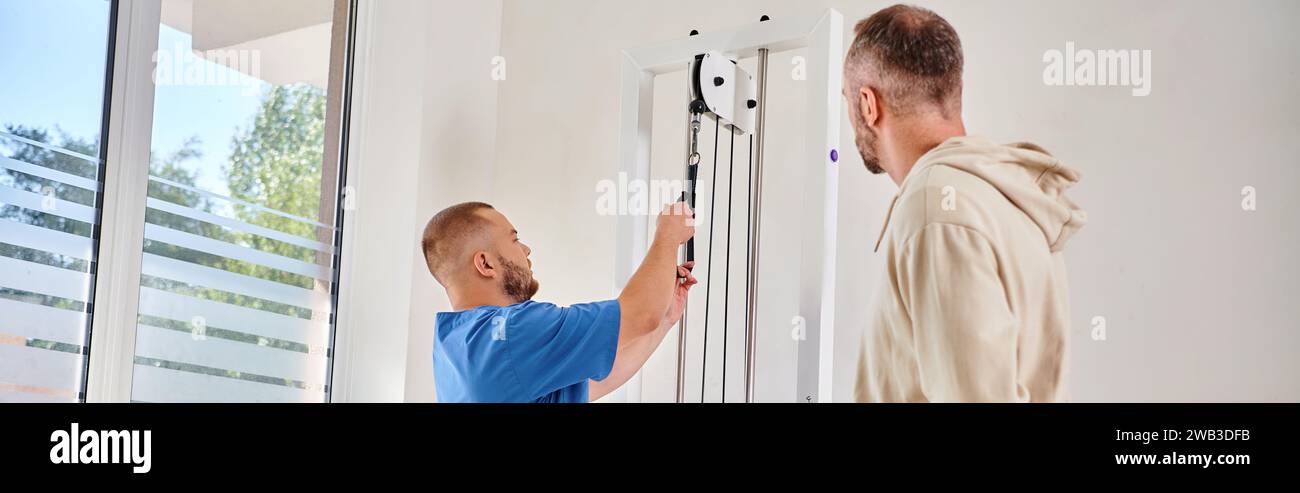 rehabilitologist in blue uniform showing training equipment to man in ...