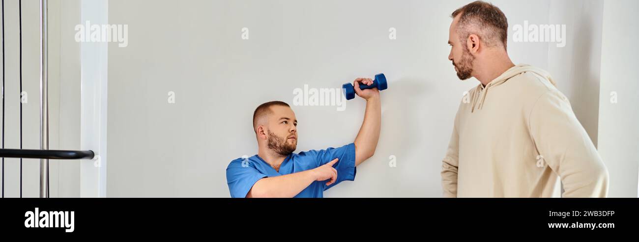 young rehabilitologist showing how to train arm with dumbbell to man in ...