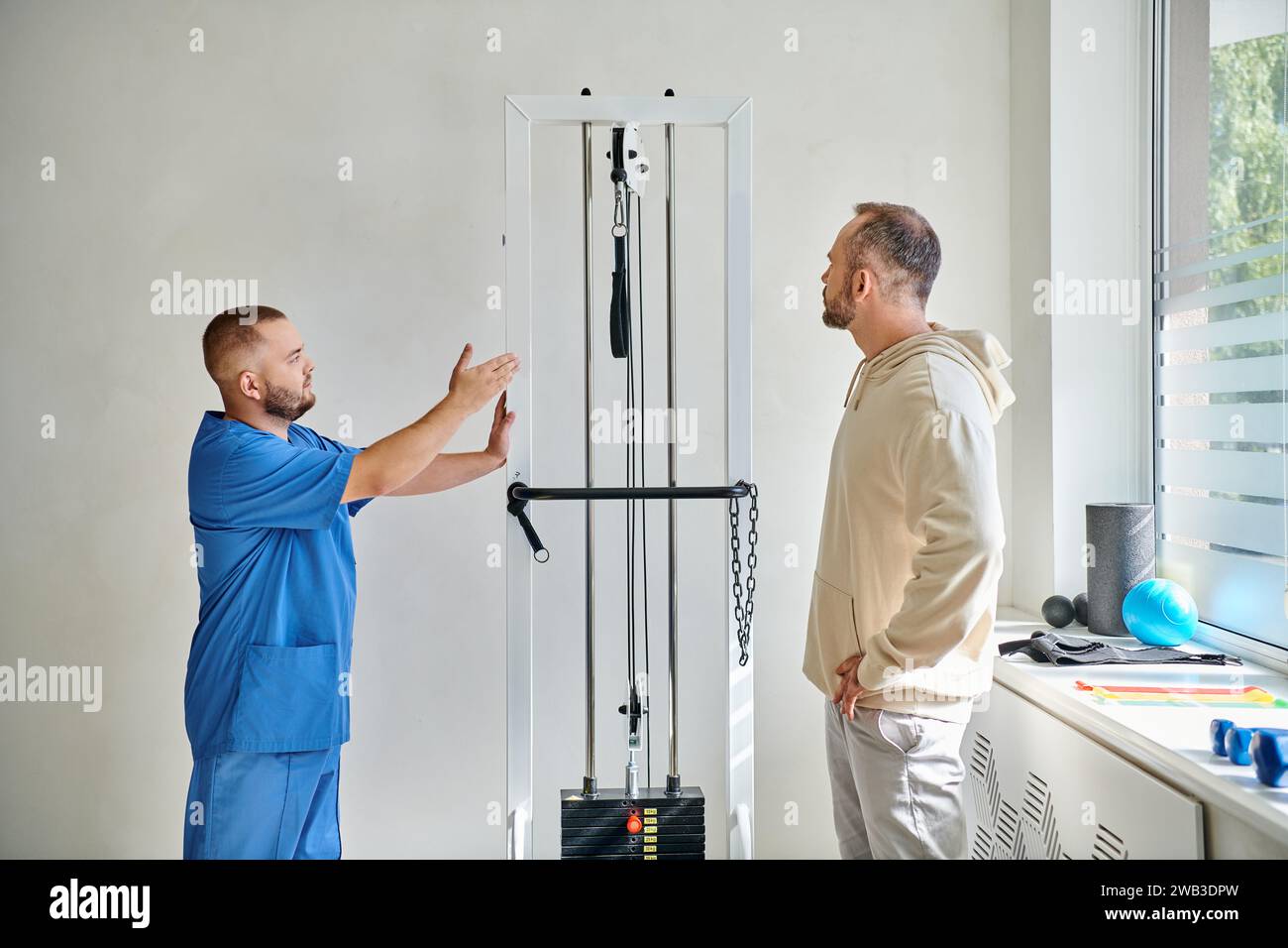 rehabilitologist in blue uniform showing exercise equipment to his ...