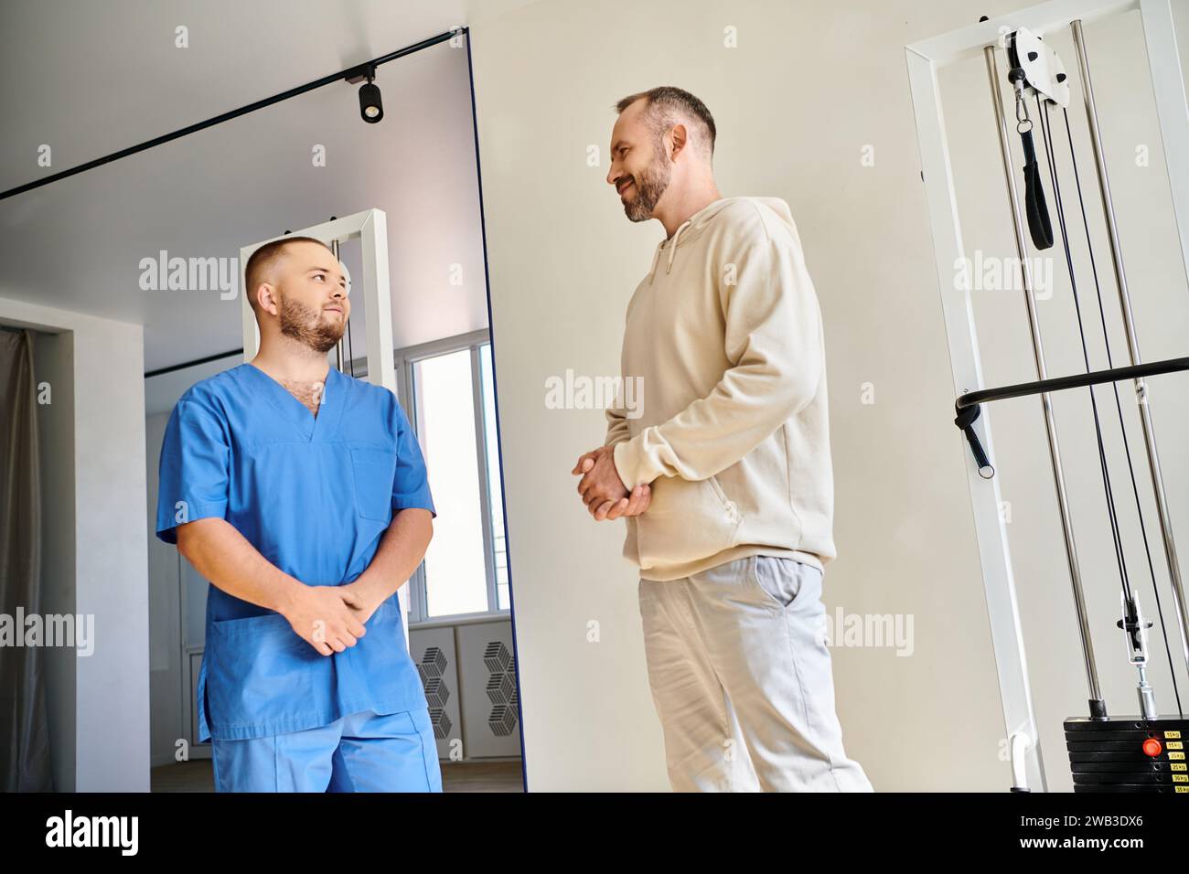experienced rehabilitologist in blue uniform talking to male patient in ...
