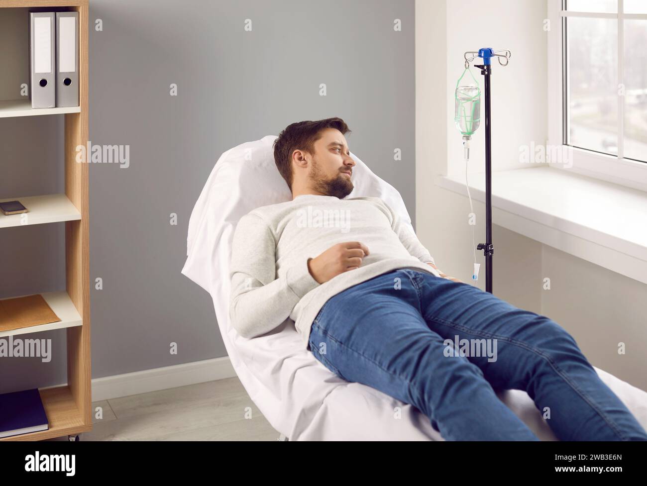 Man lying on the couch in clinic and receiving IV drip infusion and ...