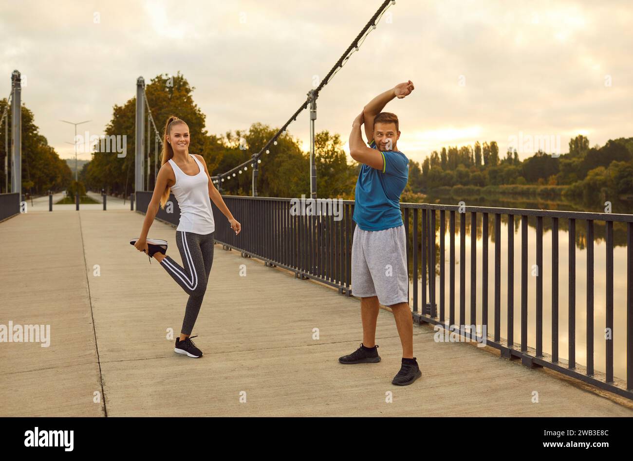 Two happy people standing on the bridge and doing warming up stretching ...