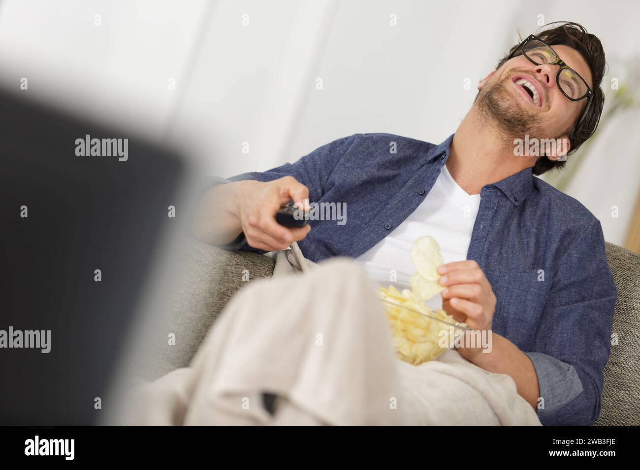 guy with remote control laughingat the television Stock Photo - Alamy