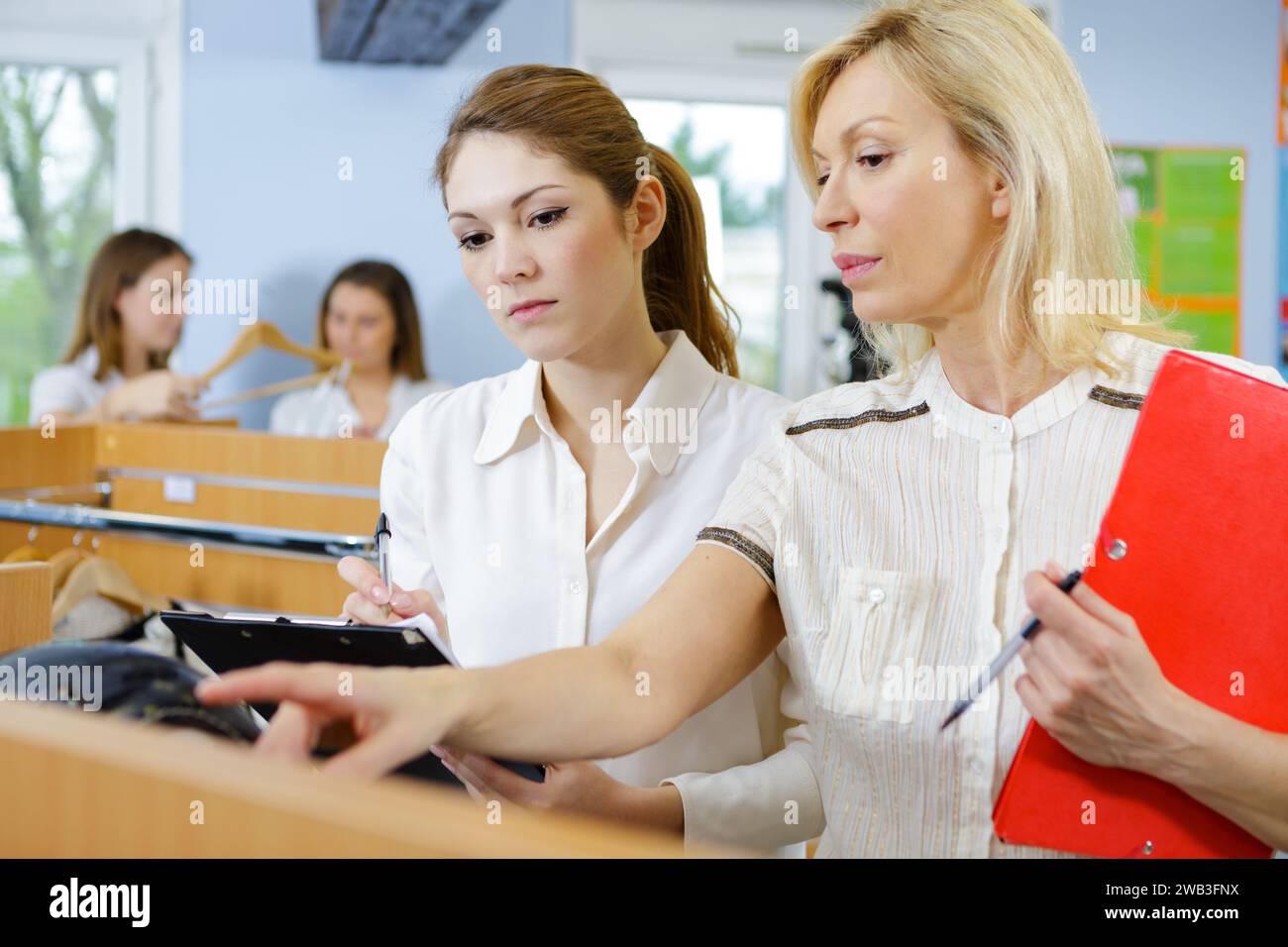 two women smiling behind the counter in clothing store Stock Photo - Alamy