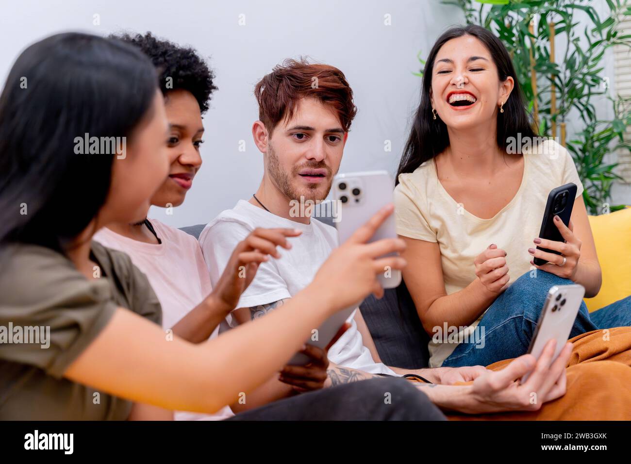 Group of lively friends laughing and sharing smartphone screens on a ...