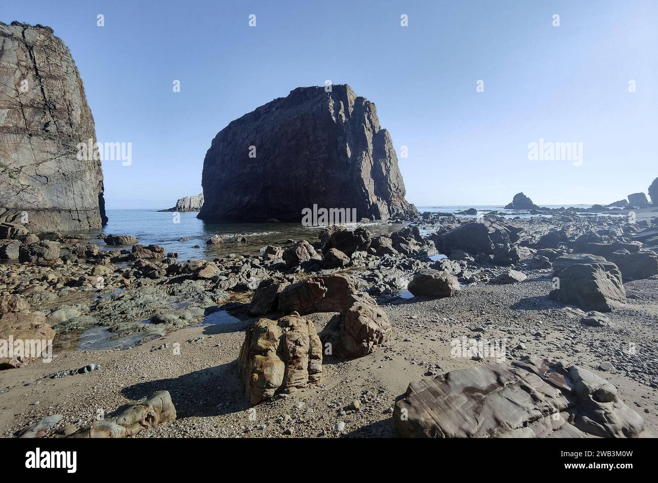 rocky shoreline with large, rugged formations jutting out from the sea ...