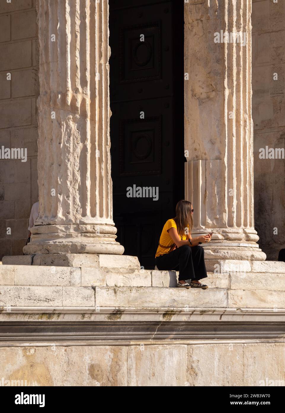 Nimes, France - october 4, 2023: young lady sitting between the pillars ...