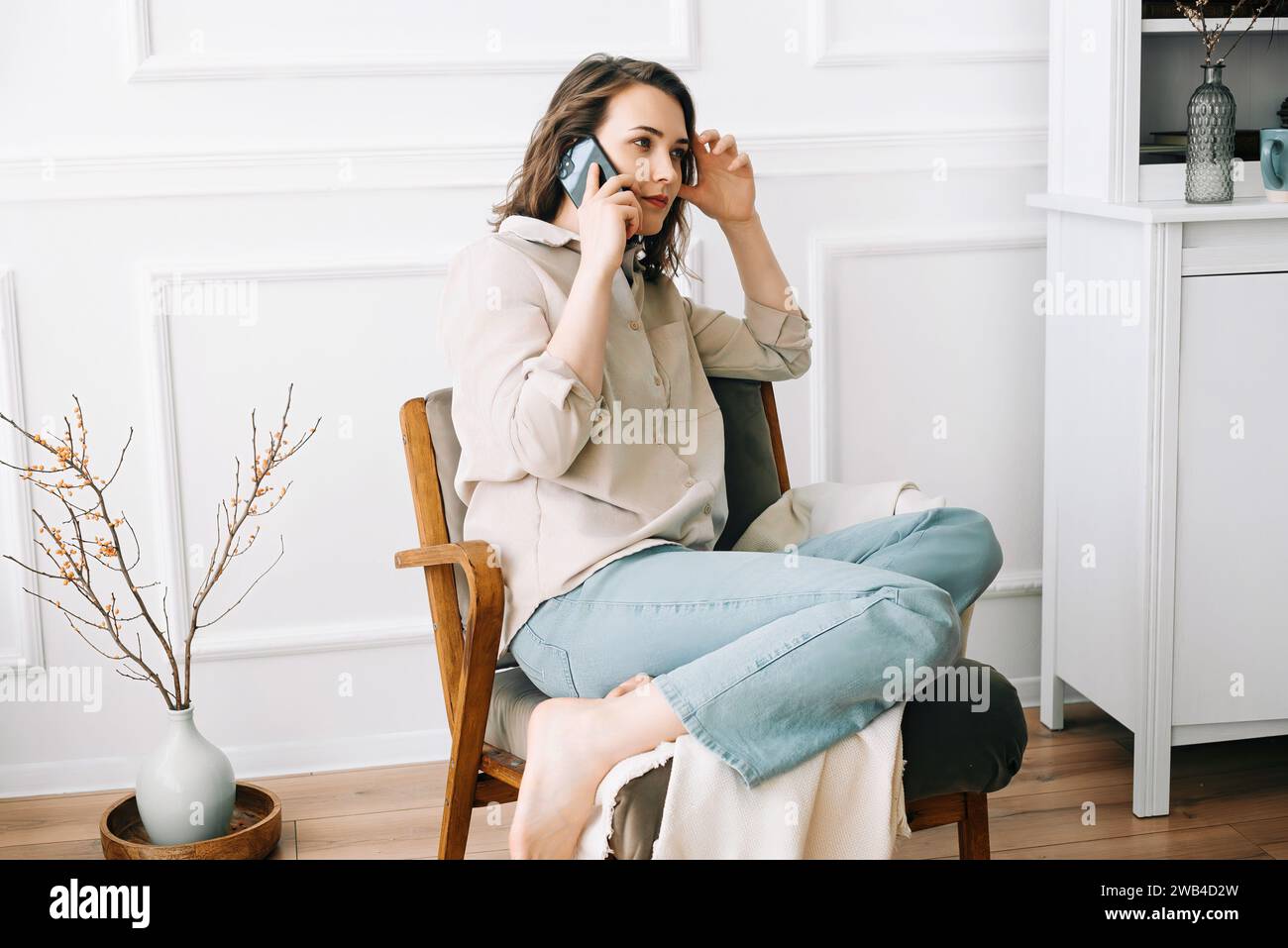 Serious millennial woman talks on the phone, sitting on a chair and ...