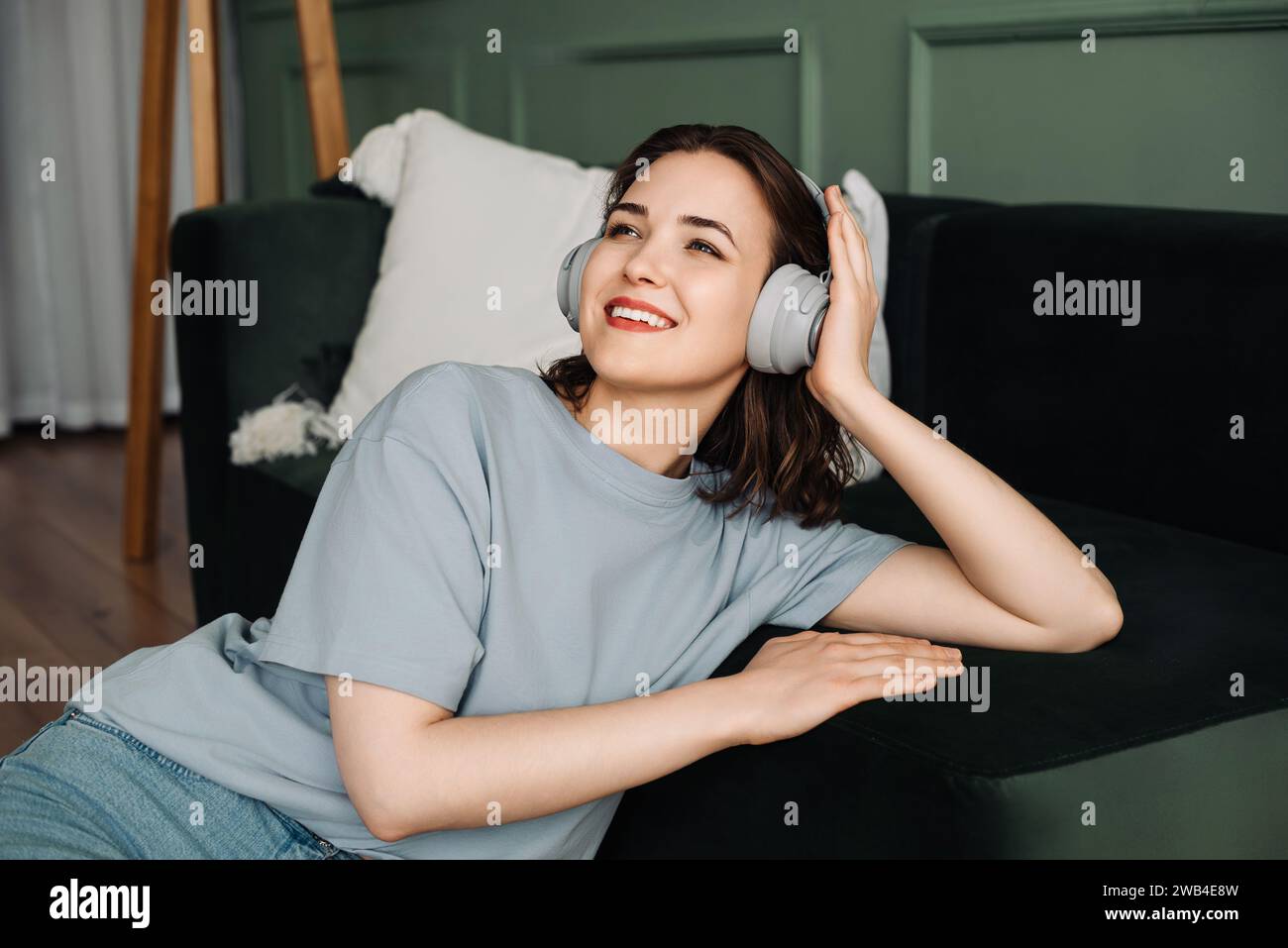 Thoughtful joyful young woman wearing wireless headphones listening to ...