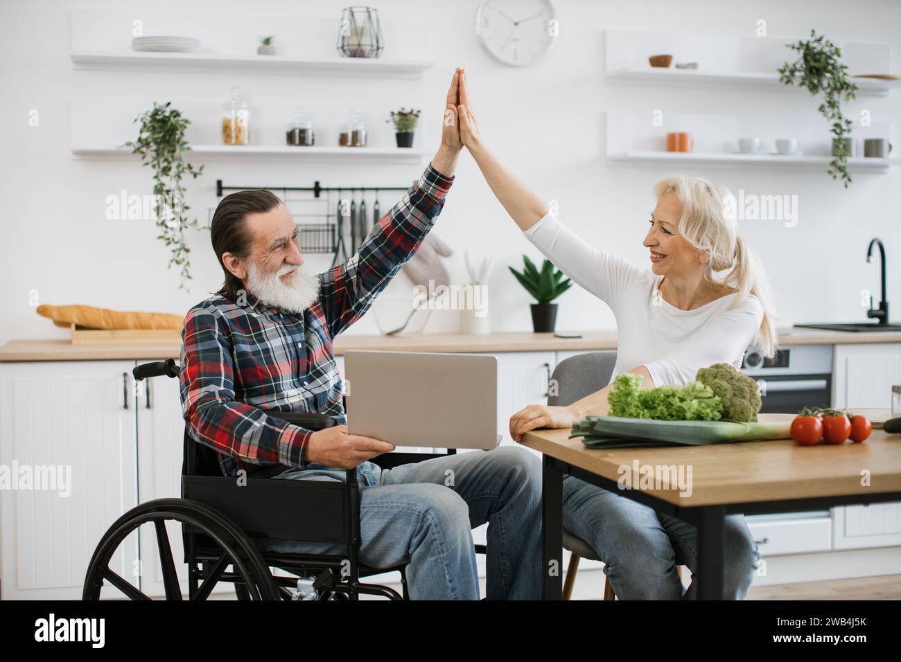 Old disabled man sitting in wheelchair and giving high five to his wife ...