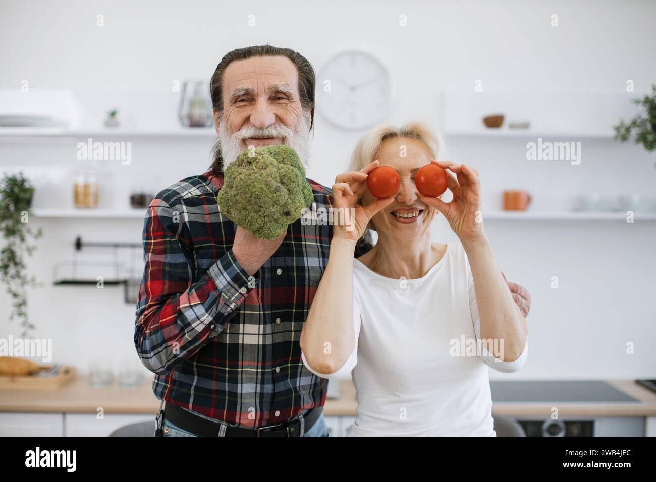 Positive senior couple man and blonde woman having fun with vegetables ...