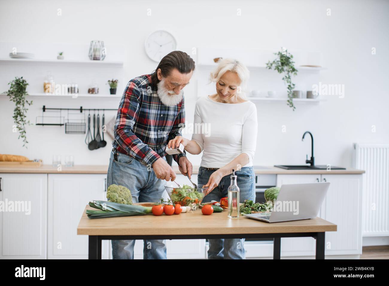 Old man mixing pieces of chopped vegetables while his wife sprinkles ...