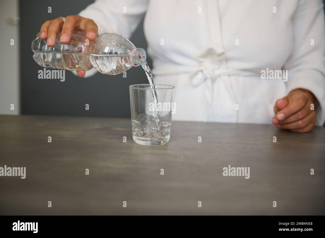 Close-up female hands pouring mineral water from a bottle into a drinking glass. Young woman ...