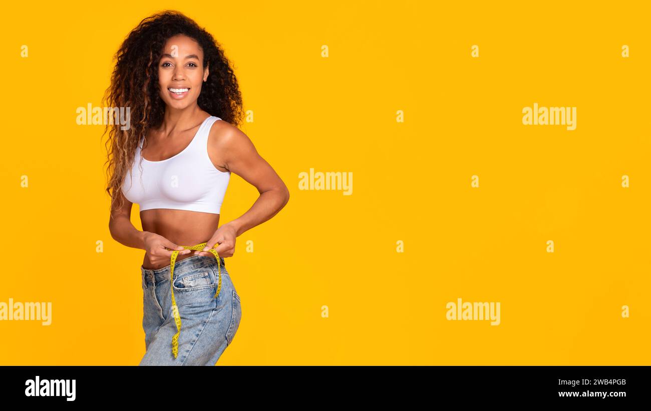 Slim african american woman measuring waist with tape, yellow backdrop ...