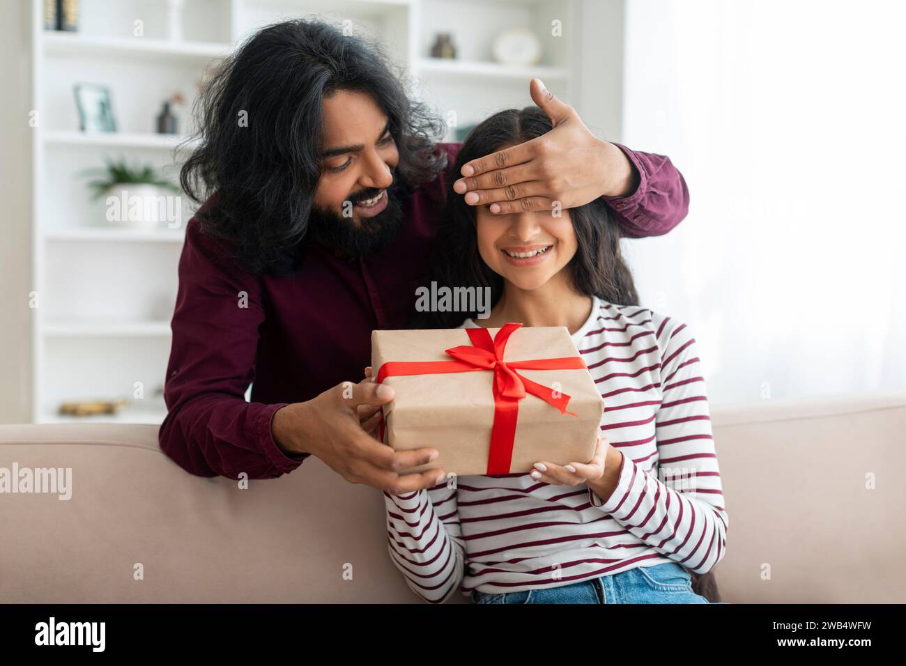 Loving millennial indian guy closing his wife eyes, giving gift box ...