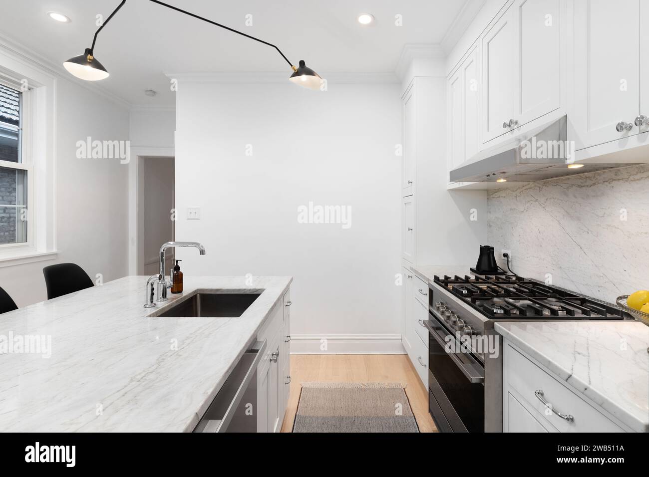 A white kitchen detail with marble countertops and backsplash, a black ...