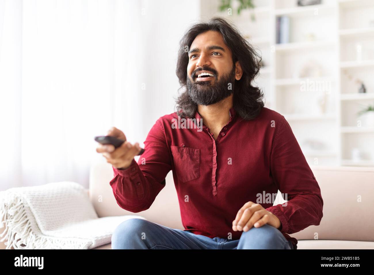 Positive indian guy with remote control in hand watching TV Stock Photo ...