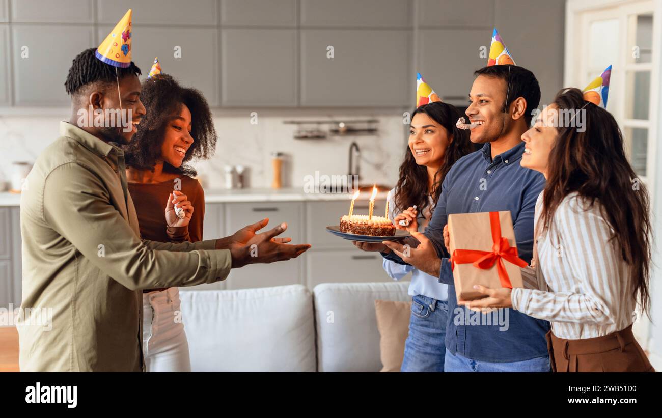 Joyful group of friends giving birthday cake to guy indoor Stock Photo ...