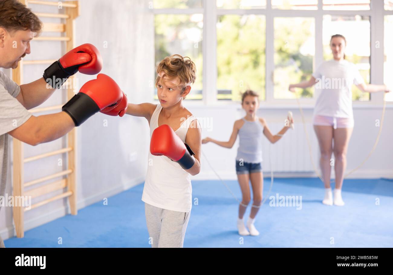 Preteen boy practicing boxing punches in sparring with father in gym ...
