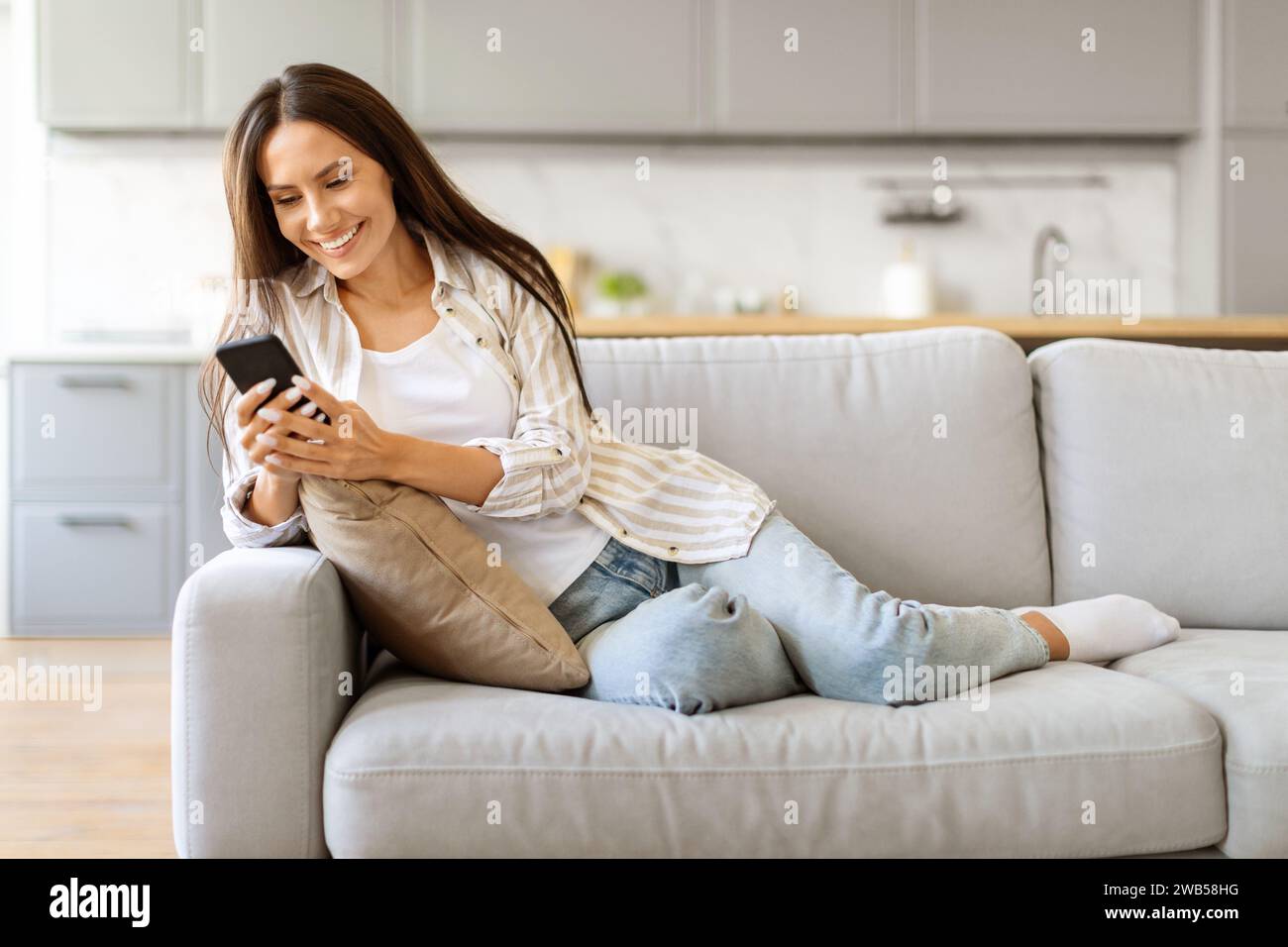 Contented female enjoying browsing her smartphone, sitting on couch in ...