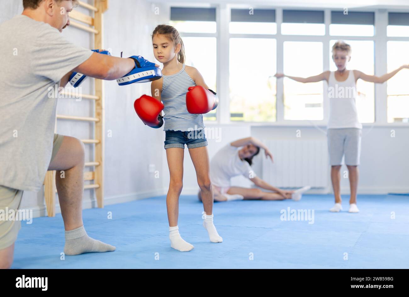 Girl with her trainer father at gym. Boy wearing boxing gloves exercise ...