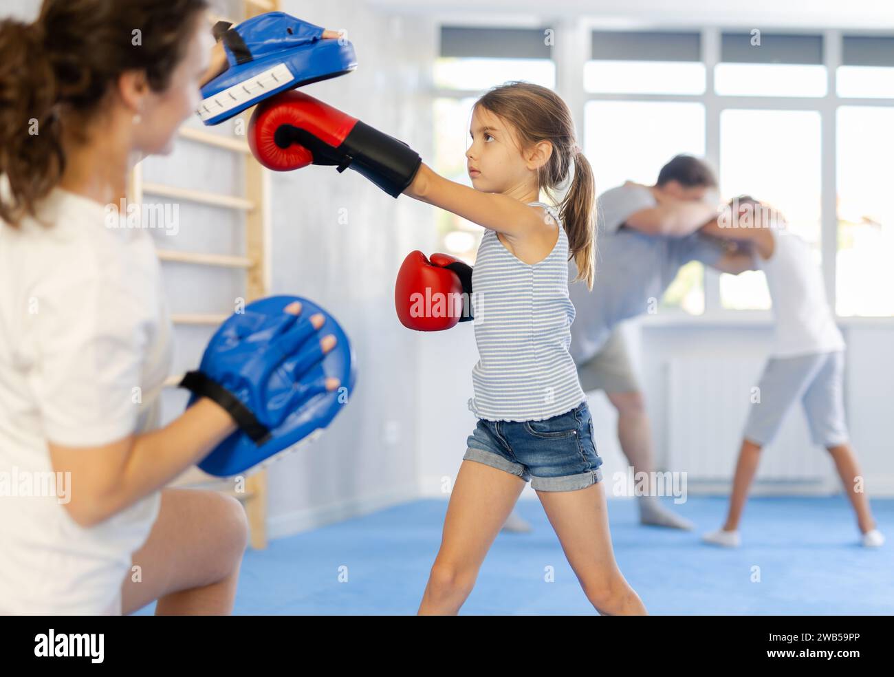 Girl and mom are boxing in gym, mother helps child to work out force of ...
