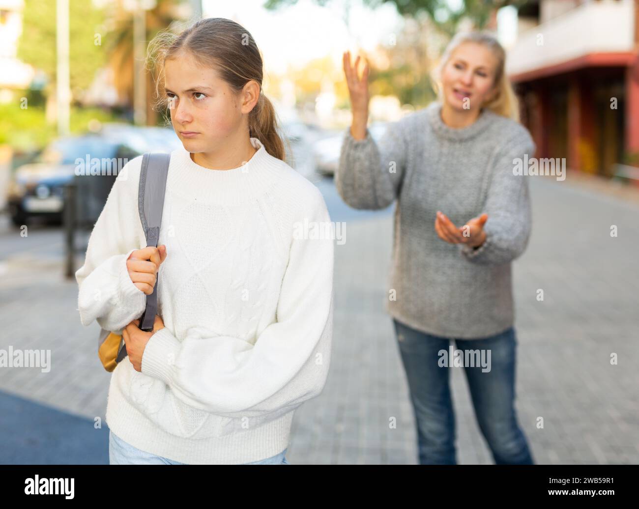 Upset teen girl walking on city street with worried mother reproaching ...