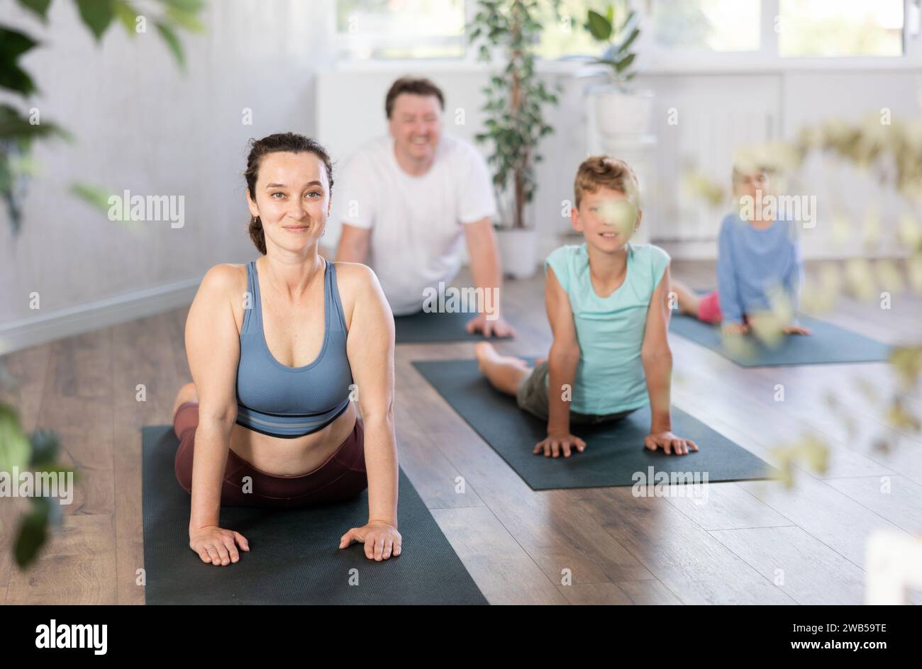 Willing middle-aged woman practicing cobra pose of yoga with her family ...
