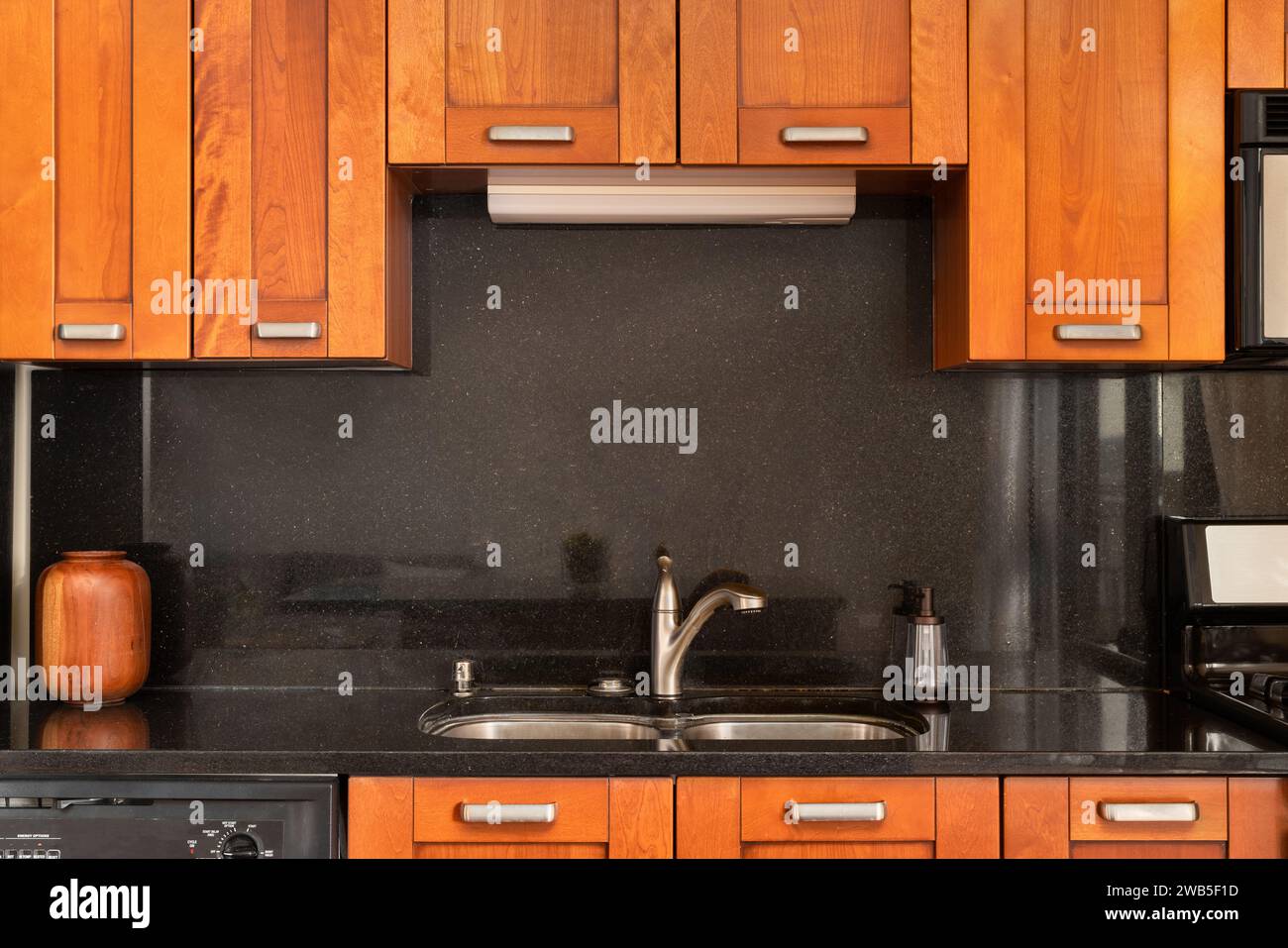 A kitchen faucet detail with wood cabinets and a black galaxy granite ...