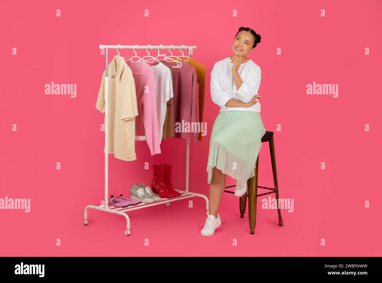 Fashion Idea. Pensive Smiling Asian Woman Sitting Near Clothing Rack ...
