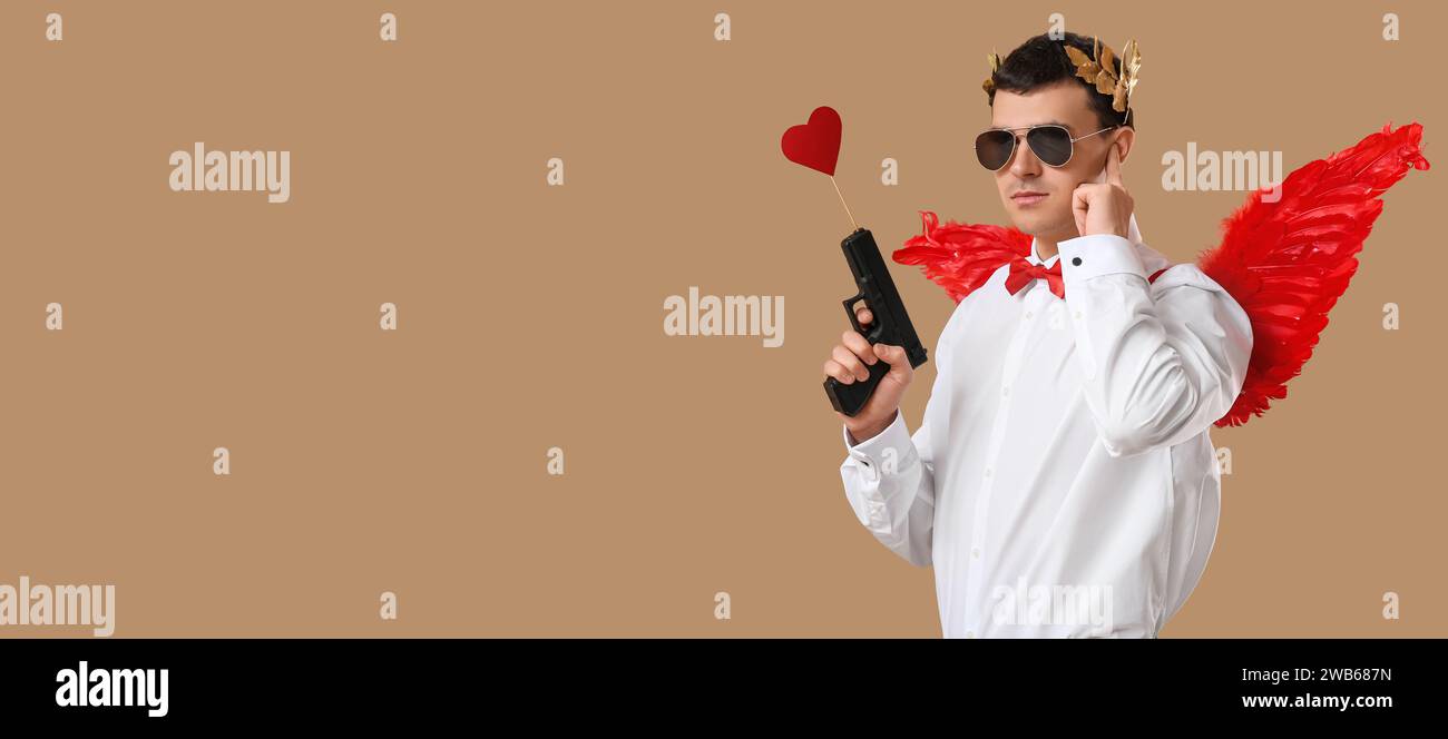Cool young man dressed as Cupid with gun on beige background with space ...