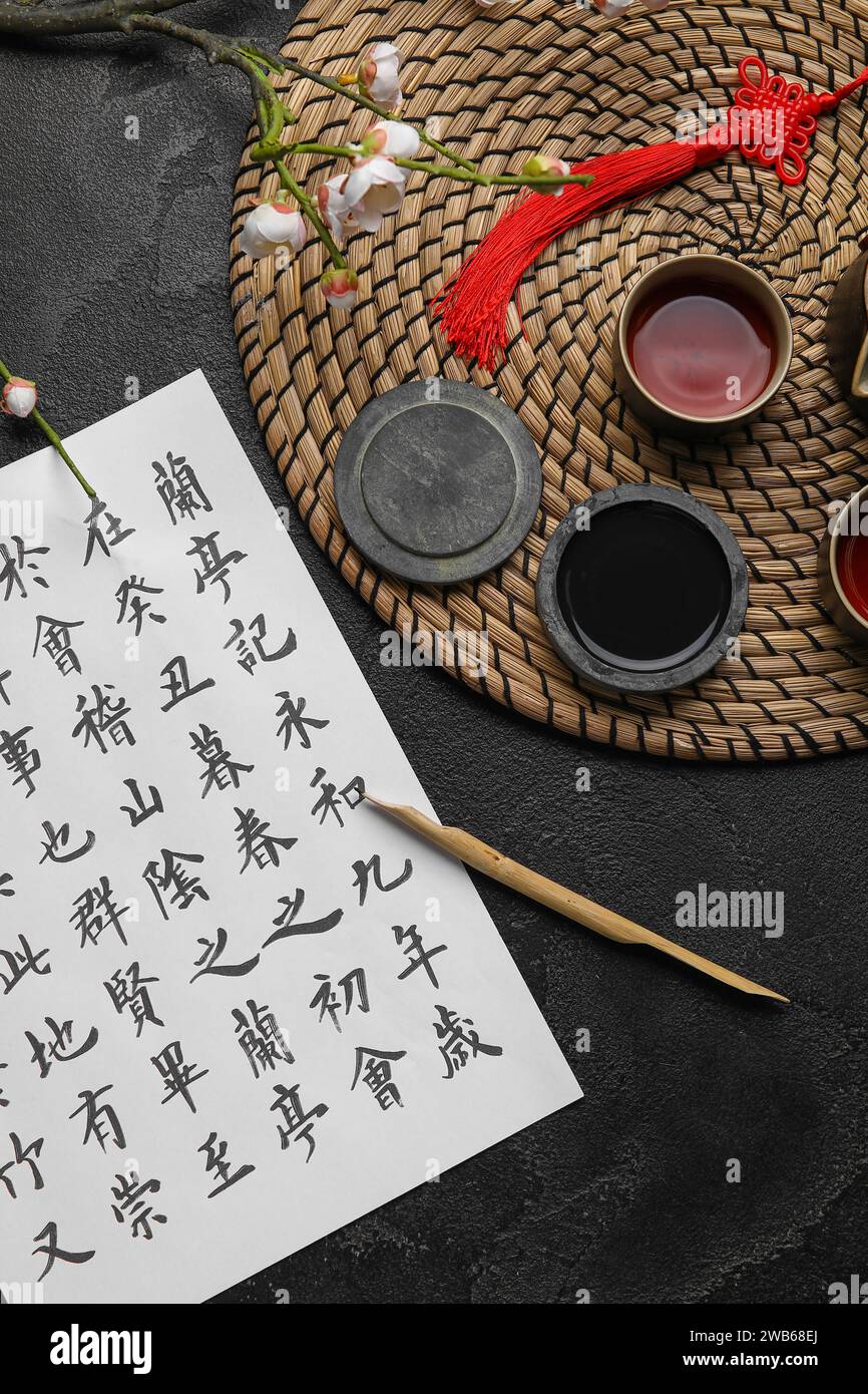 Paper sheet with Asian hieroglyphs, ink, nib pen and cups of tea on ...