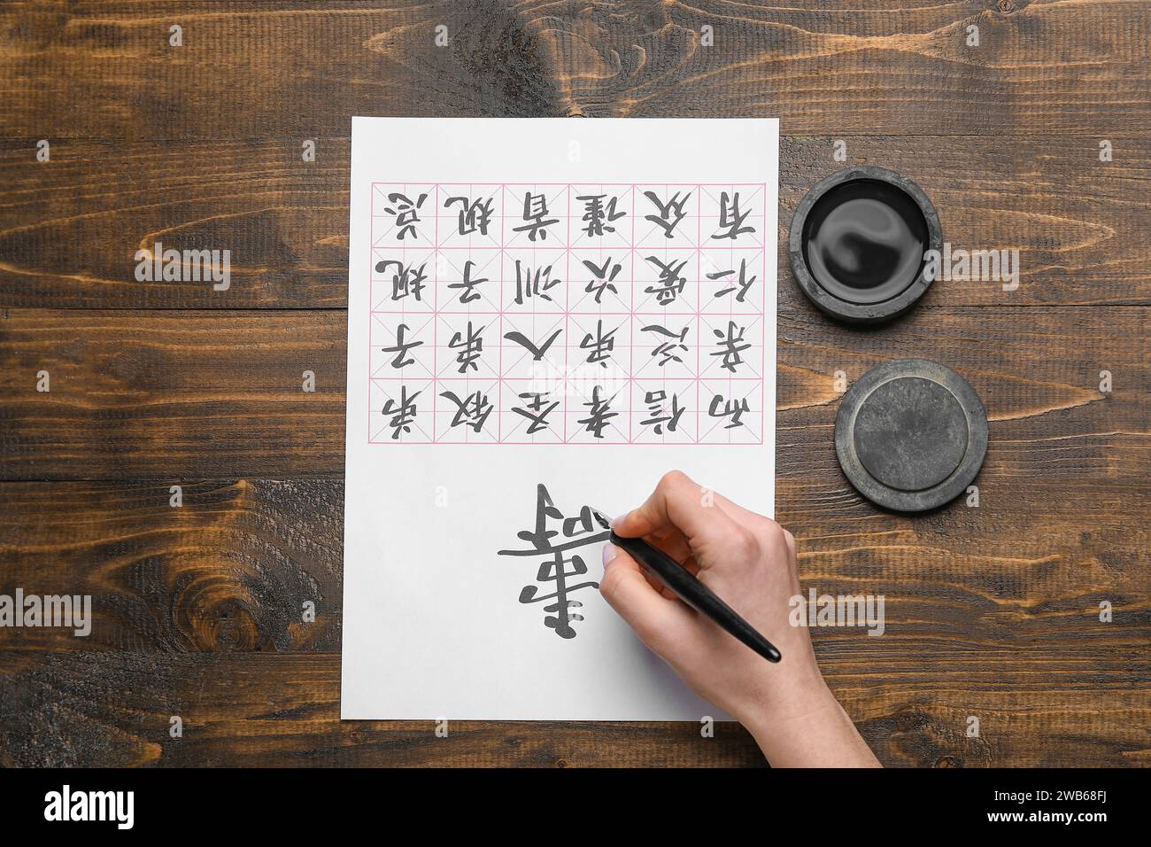 Woman writing Asian hieroglyphs on wooden background. International ...