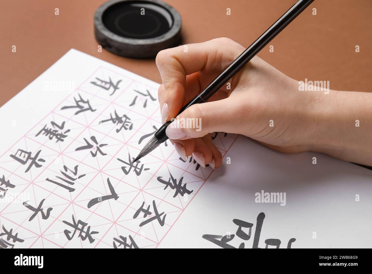 Woman writing Asian hieroglyphs on color background, closeup ...