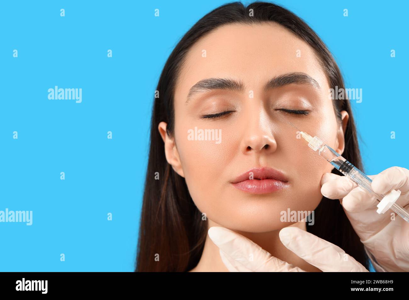 Young woman receiving filler injection in face against blue background ...