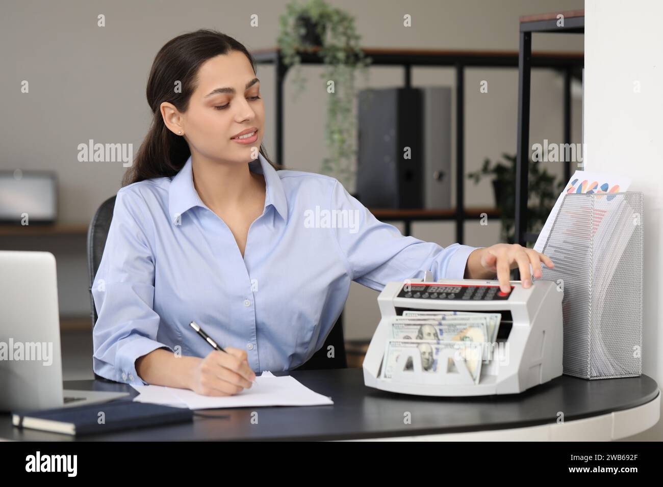 Female bank manager using cash counting machine in office Stock Photo ...
