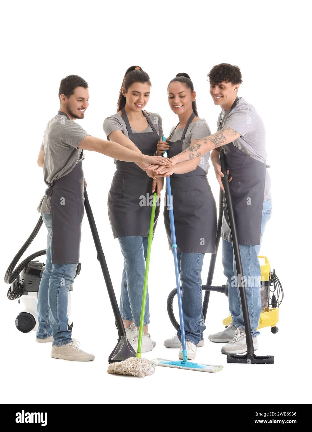 Young janitors with cleaning supplies putting hands together on white ...