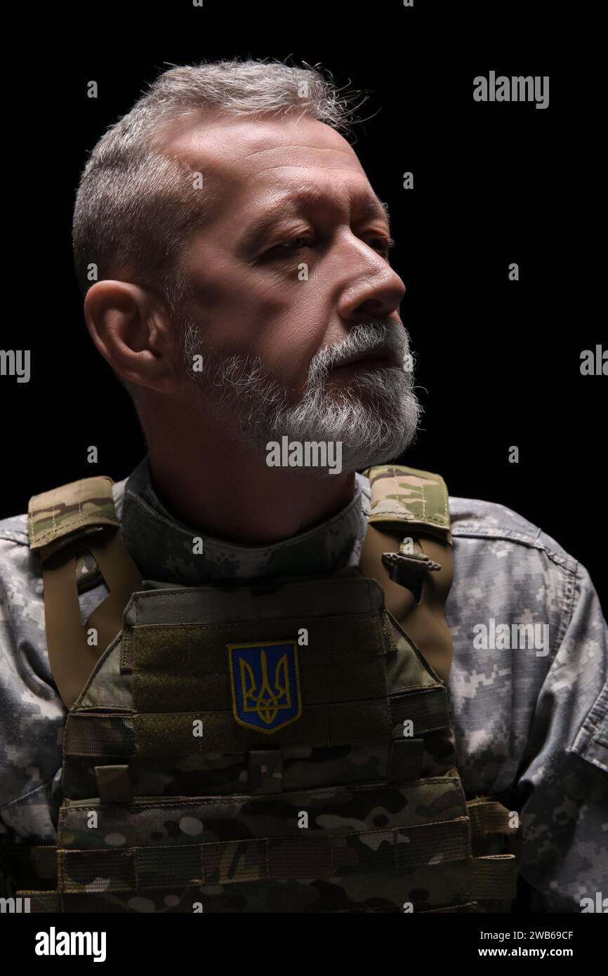 Mature soldier with Ukrainian coat of arms patch on dark background ...
