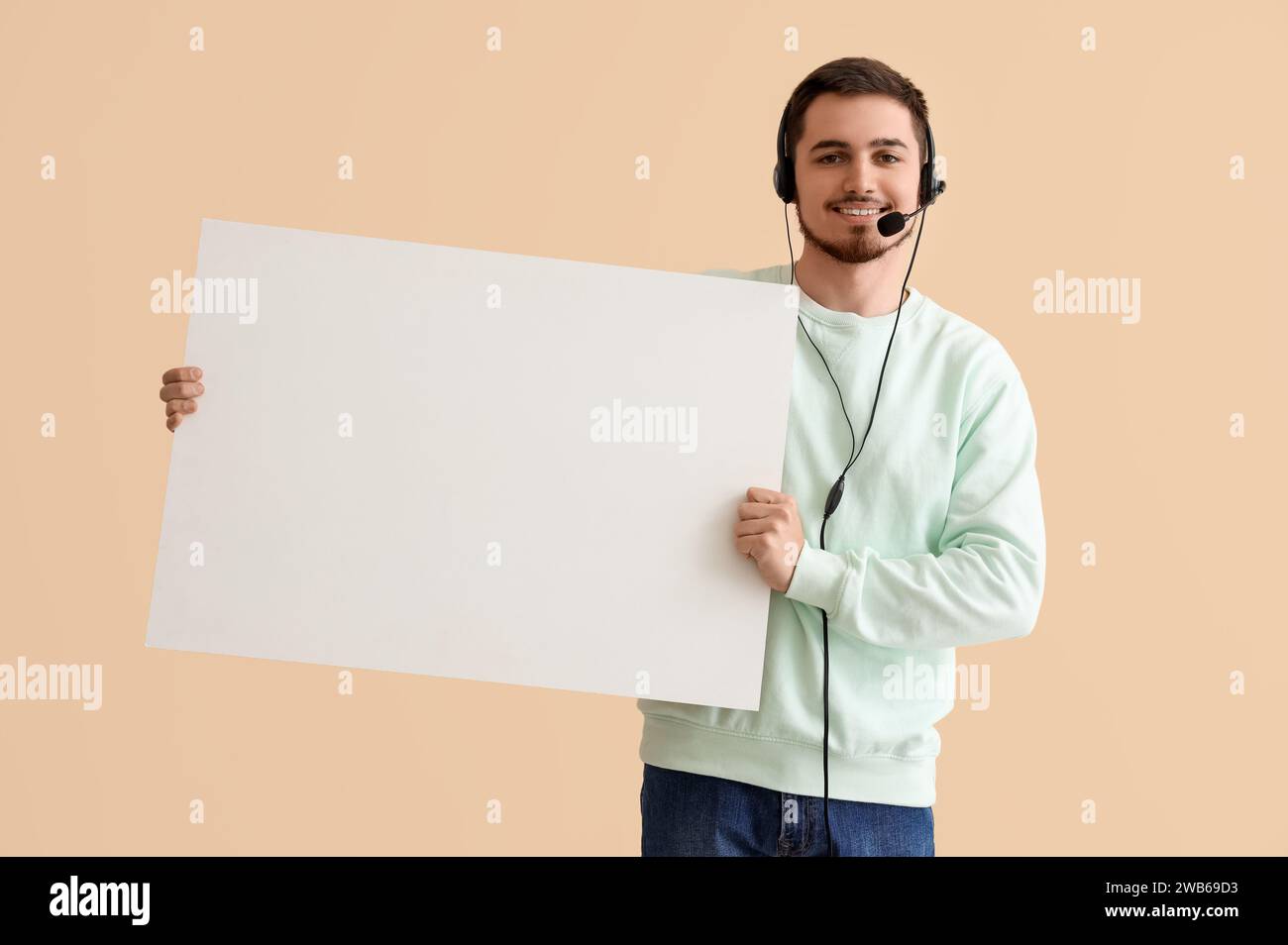 Male technical support agent with blank poster on beige background ...