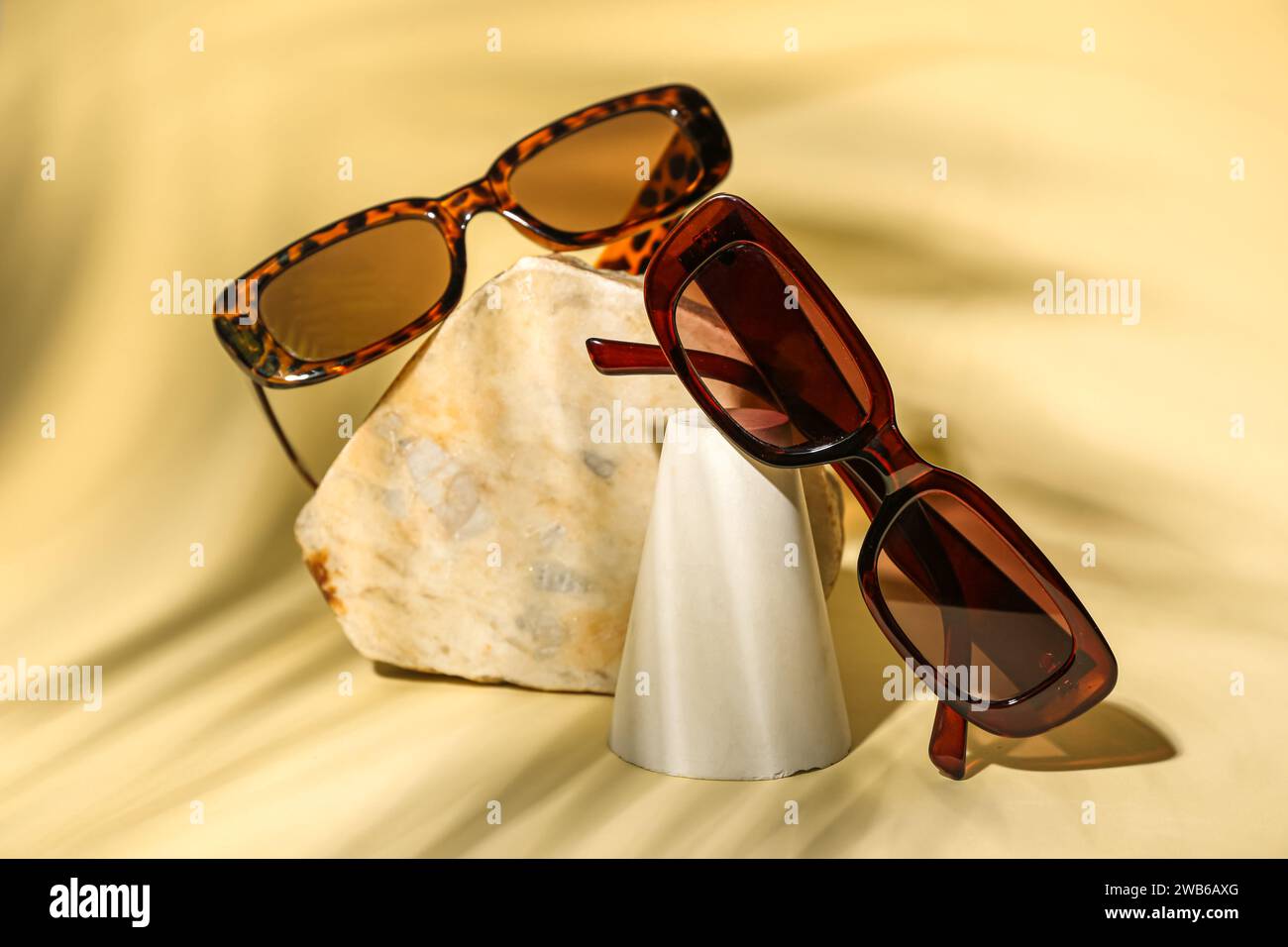 Stone and decorative podium with stylish sunglasses on yellow ...