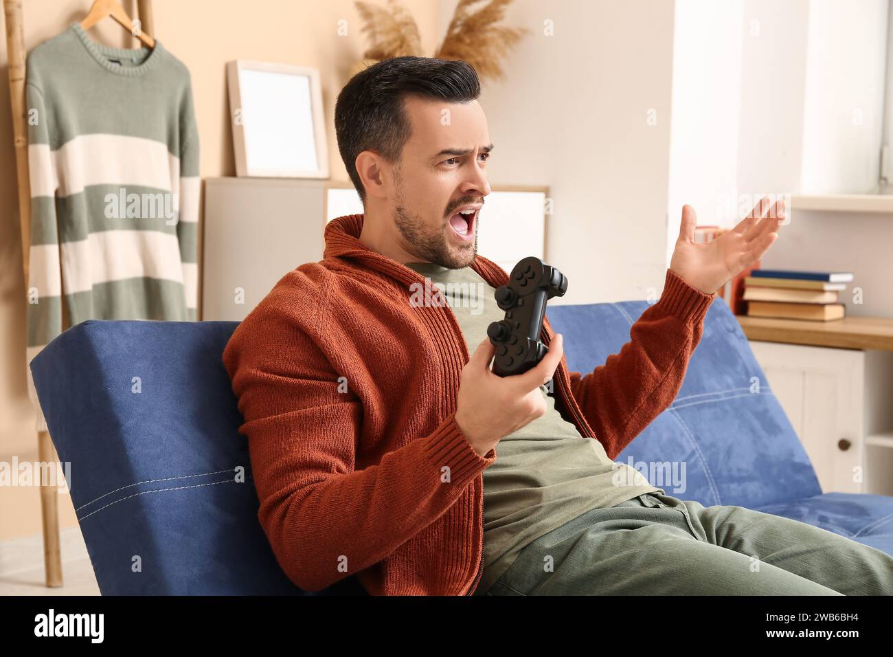 Angry young man playing video game on sofa in living room Stock Photo ...