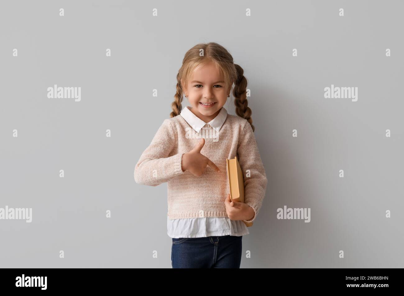 Happy little girl pointing at book on grey background Stock Photo - Alamy