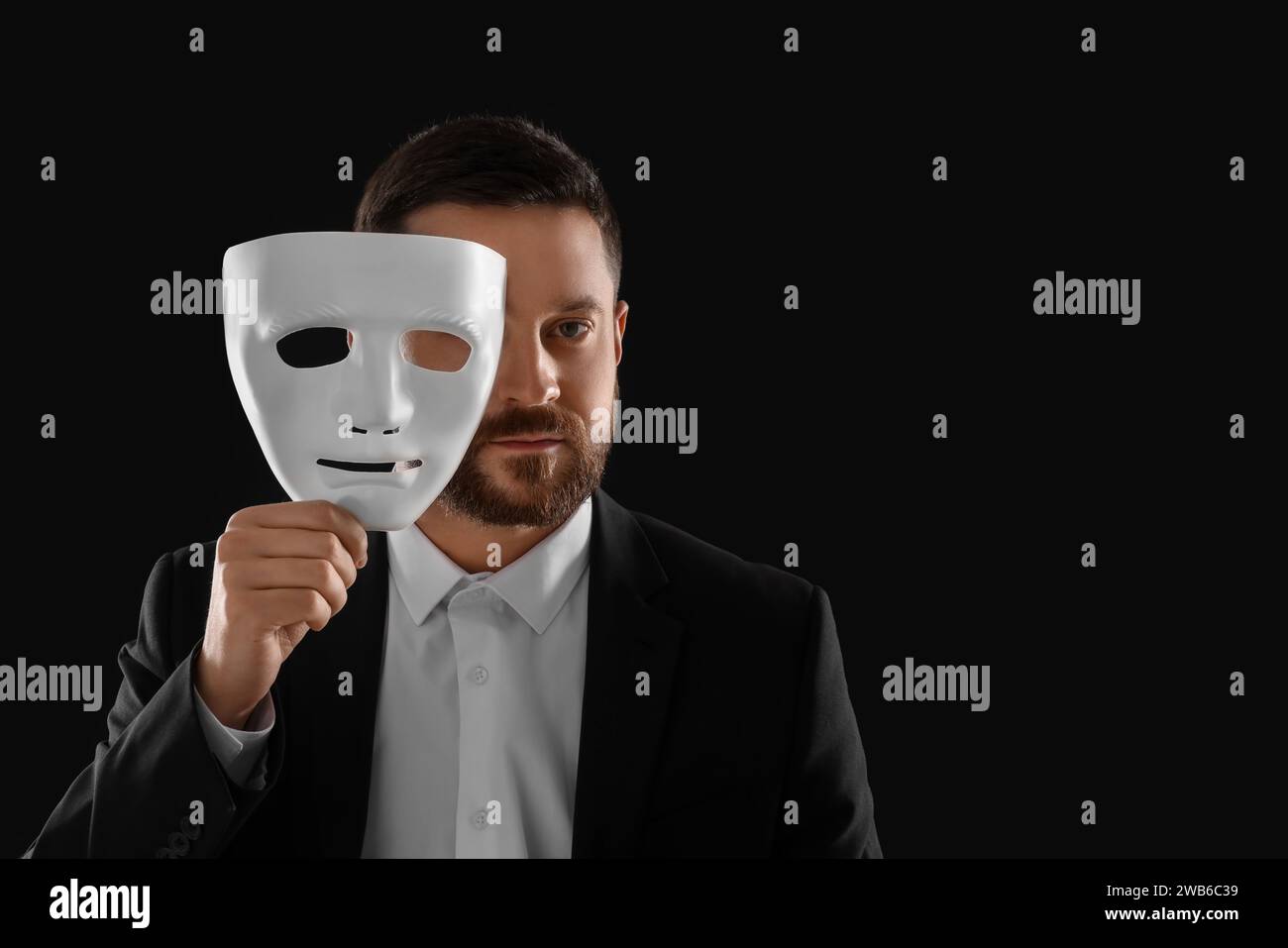 Multiple personality concept. Man covering face with mask on black ...