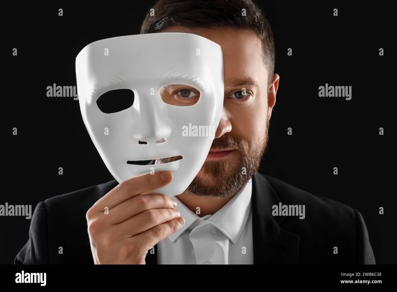 Multiple personality concept. Man covering face with mask on black ...