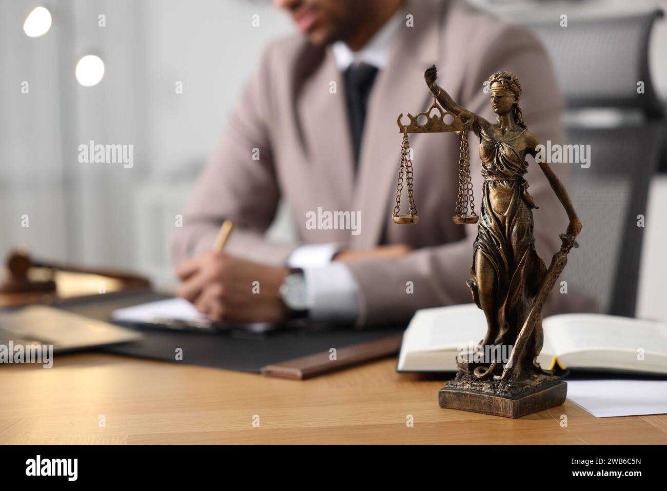 Lawyer working at table in office, focus on statue of Lady Justice ...