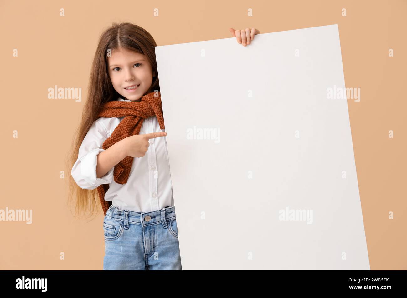 Cute little girl pointing at blank poster on beige background. Opposite ...