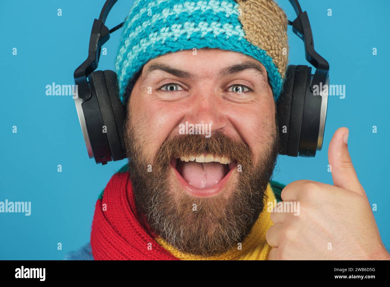 Happy Bearded Man Wearing Hat And Scarf In Headphones Showing Thumb Up