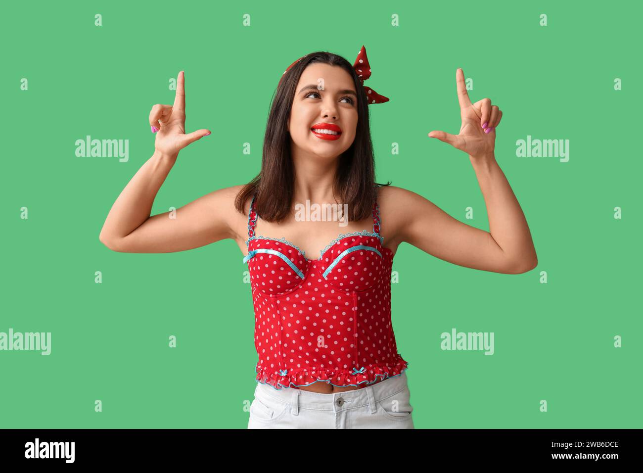 Beautiful young happy pin-up woman pointing at something on green ...