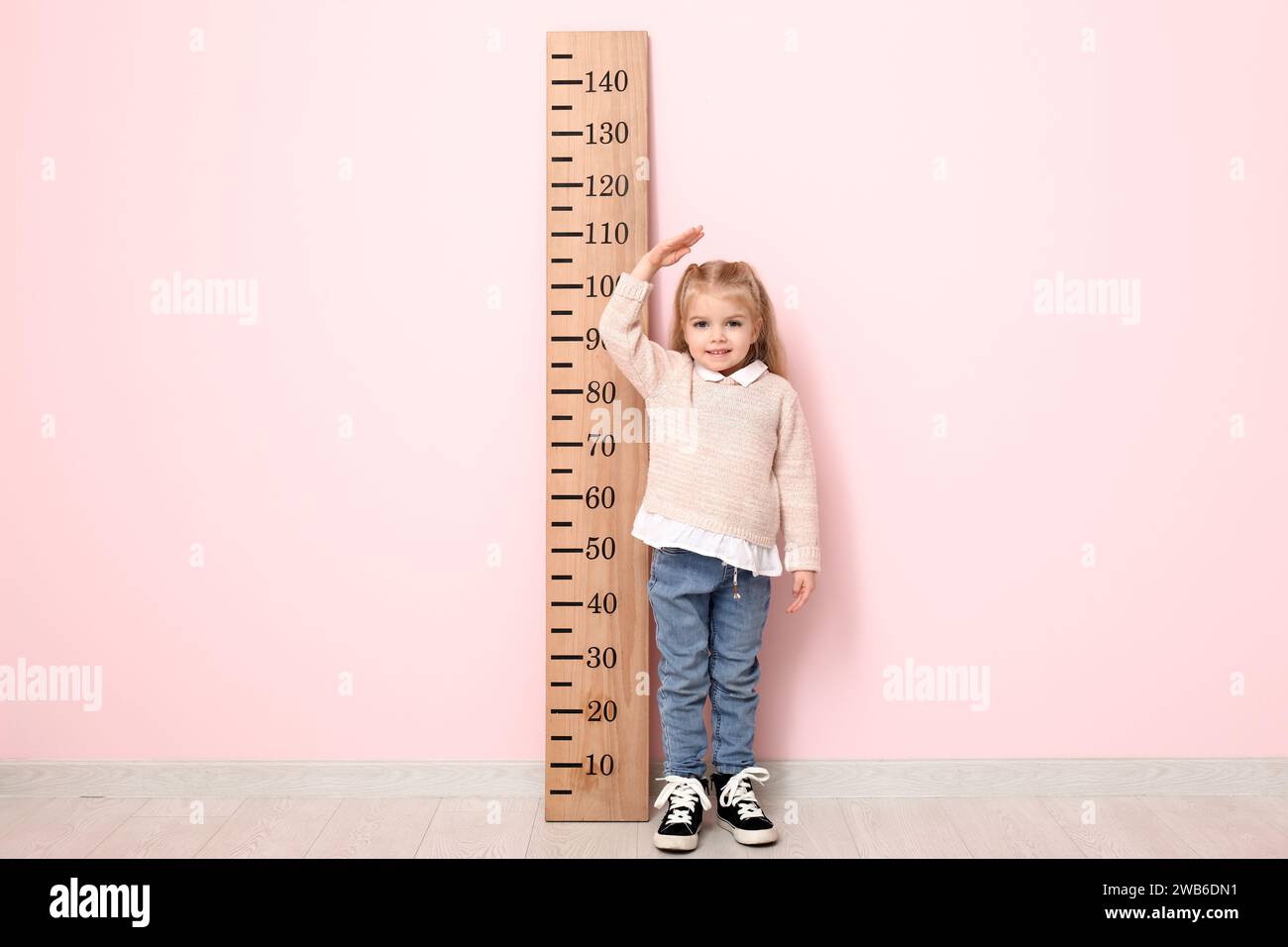 Cute little girl measuring height near pink wall Stock Photo - Alamy